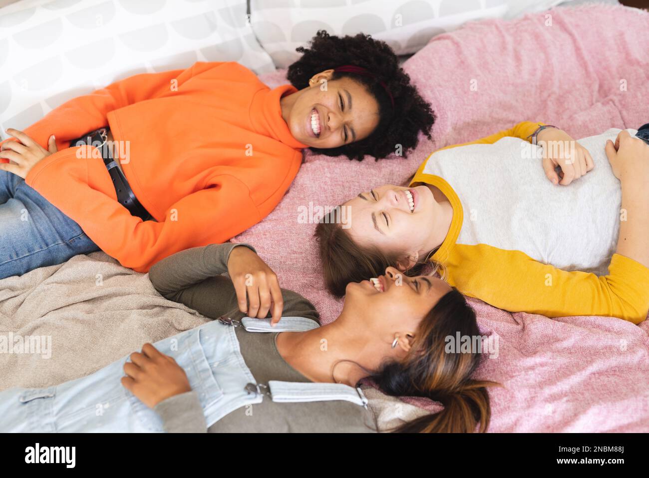 Happy diverse teenage female friends lying on bed and laughing ...