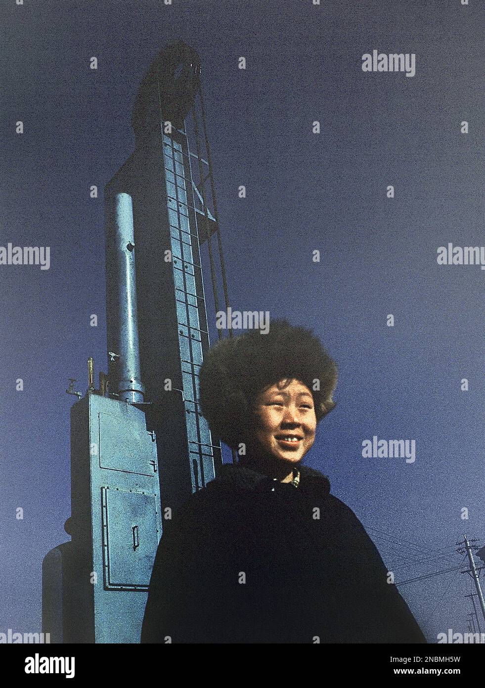 A Chinese woman oil well technician poses in front of oil pump ...