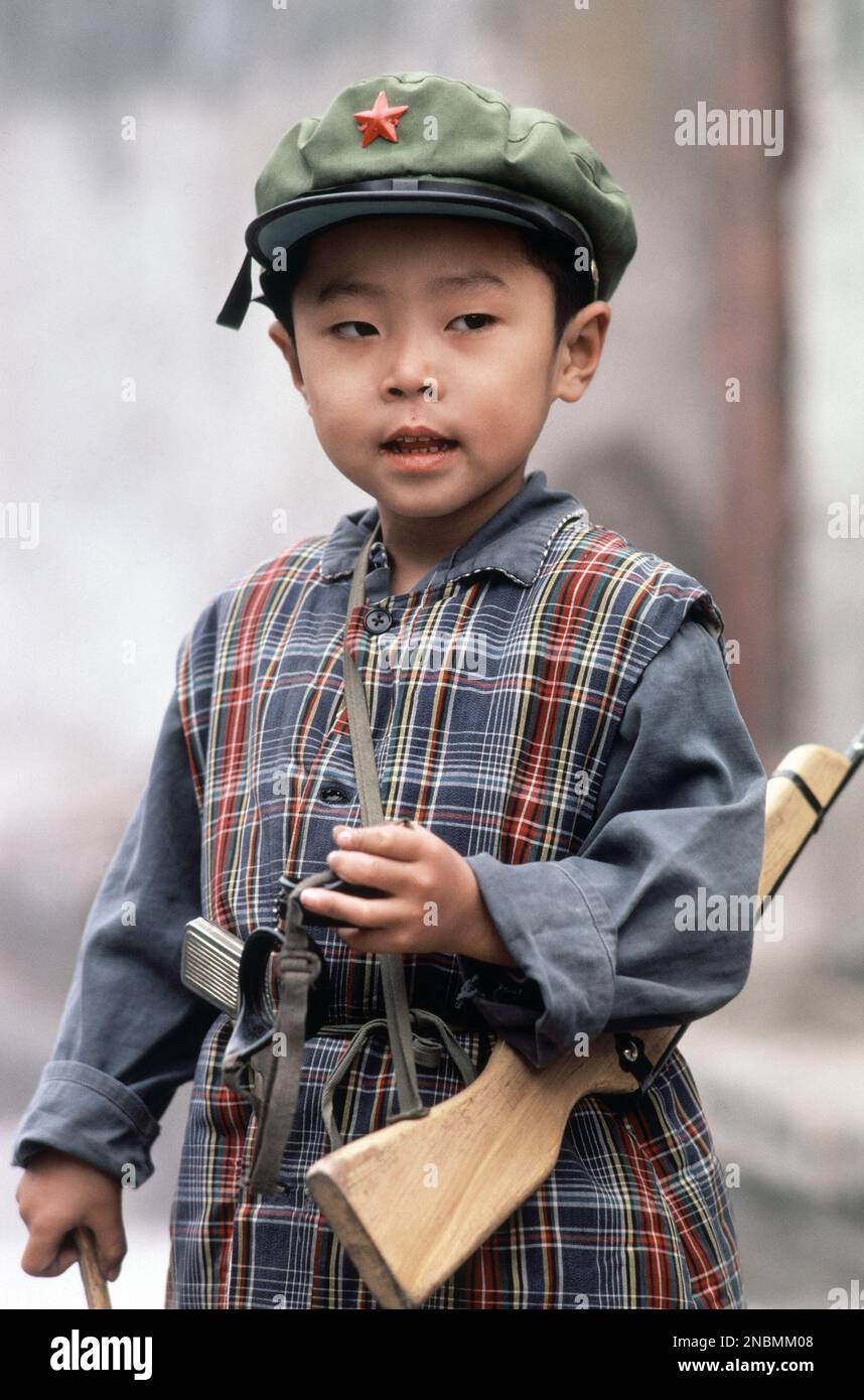 A Chinese child plays soldier with a toy rifle and pistol, in a Peking ...