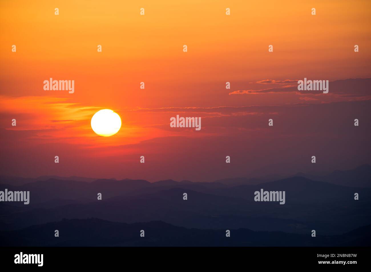 A red sun setting behind mountain and making clouds red Stock Photo - Alamy