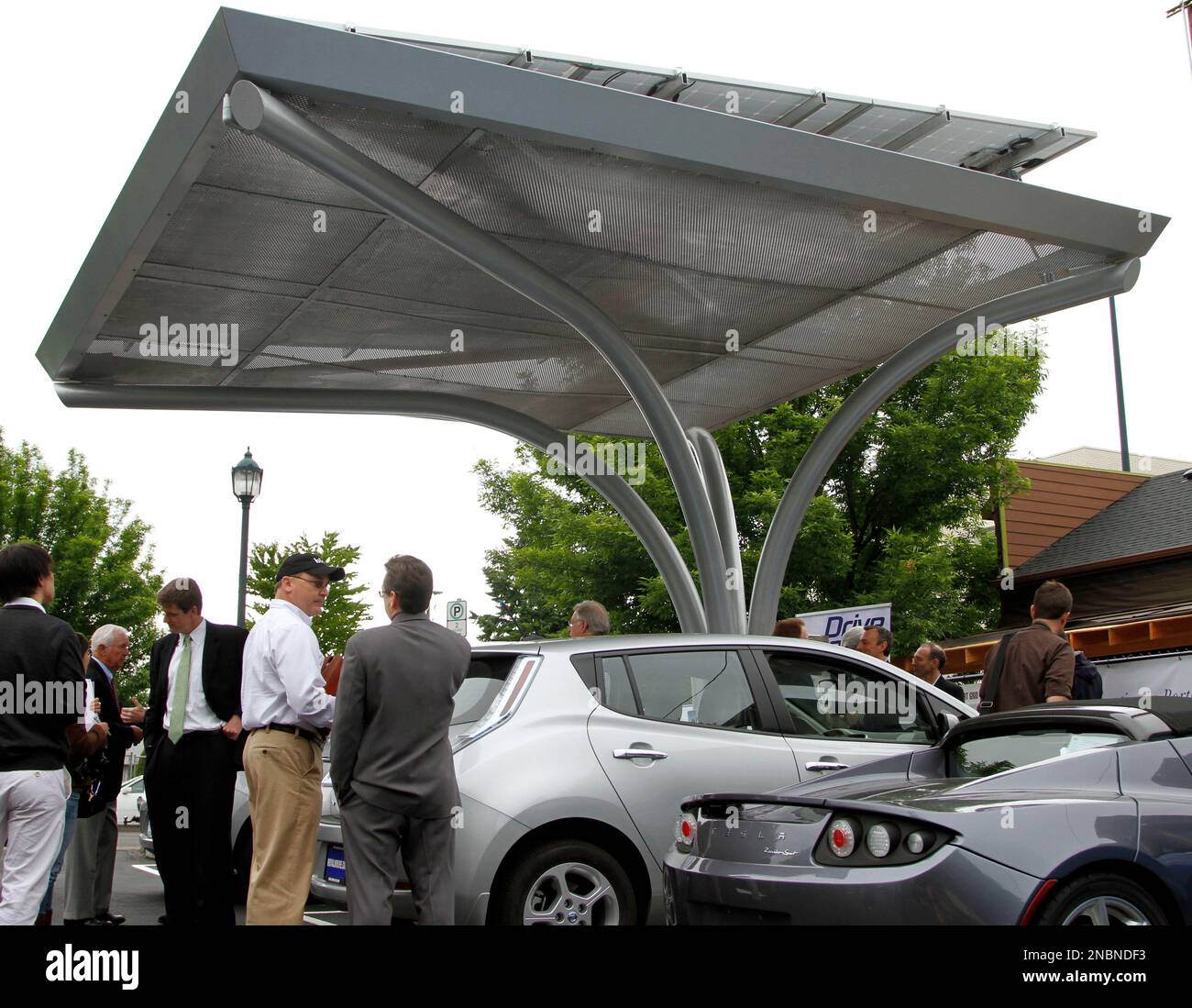 A solar canopy stands over Tesla, right, and Nissan Leaf electric cars ...