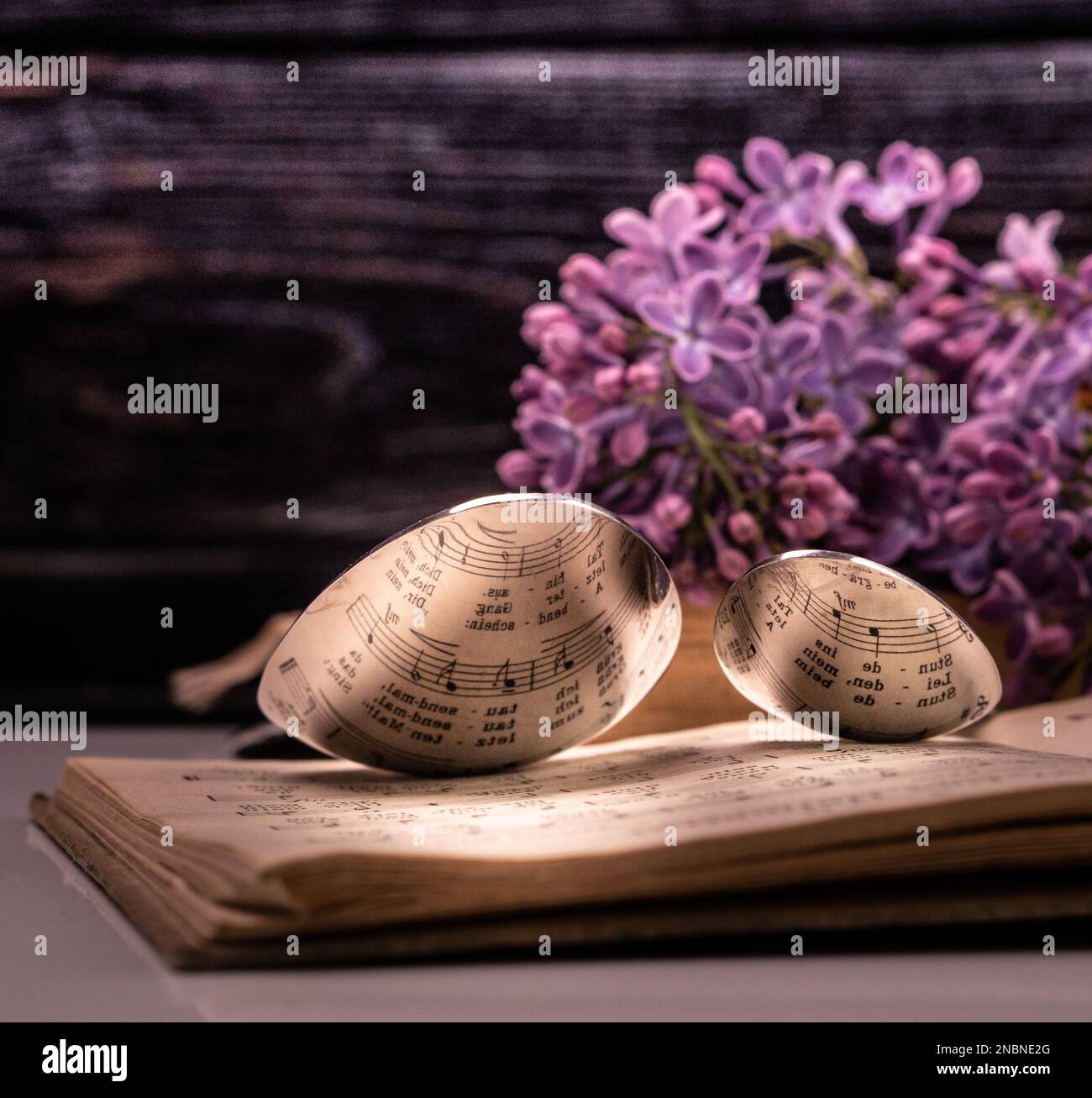 A closeup of a mirror reflecting music notes in the book, with lilac ...