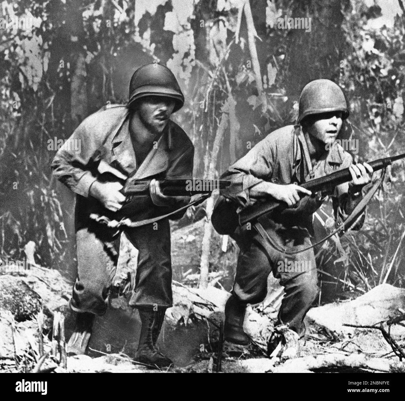 Two American riflemen plunge forward through the jungle during a ...