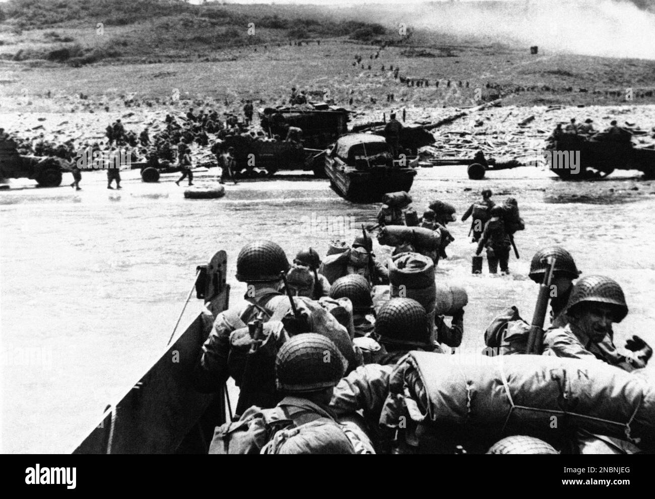 “Ducks” (amphibious trucks) and a half-track follow foot troops ashore ...