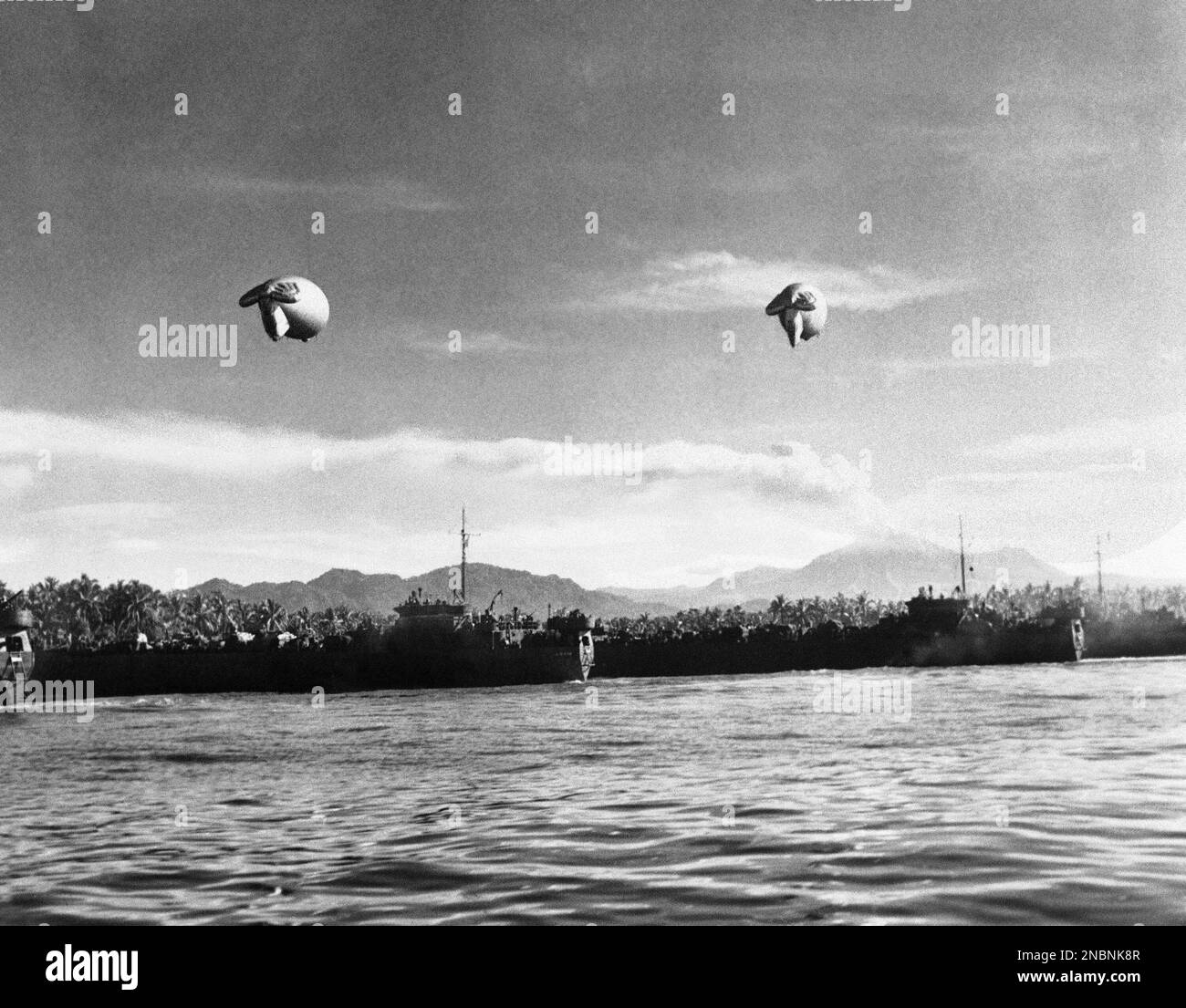 A pair of barrage ballons float in the air over several LST’s (landing ...