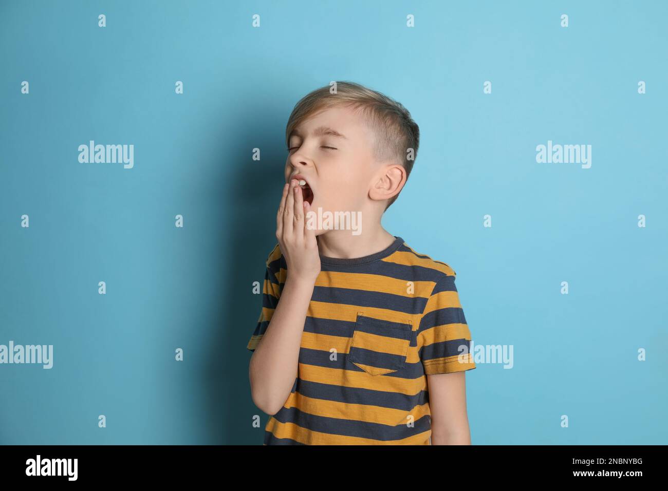 Portrait of sleepy boy yawning on turquoise background Stock Photo - Alamy