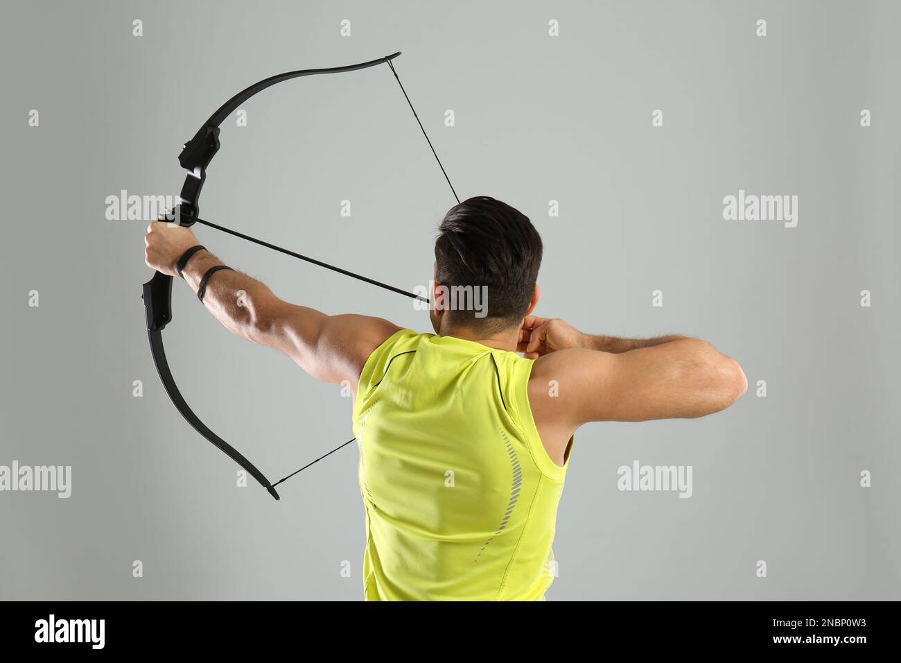 Man with bow and arrow practicing archery on light grey background ...