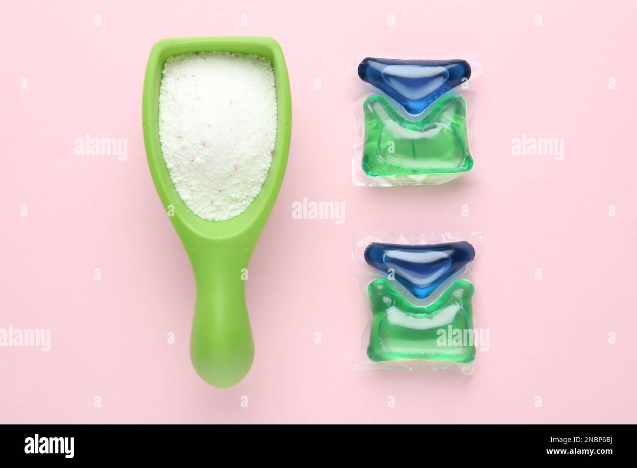 Laundry capsules and measuring scoop of washing powder on pink ...