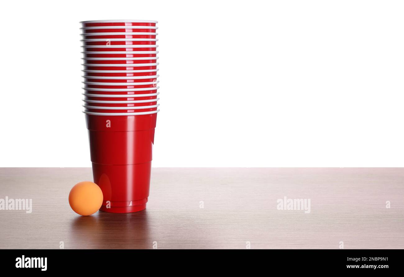 Plastic cups and ball for beer pong on wooden table against white ...