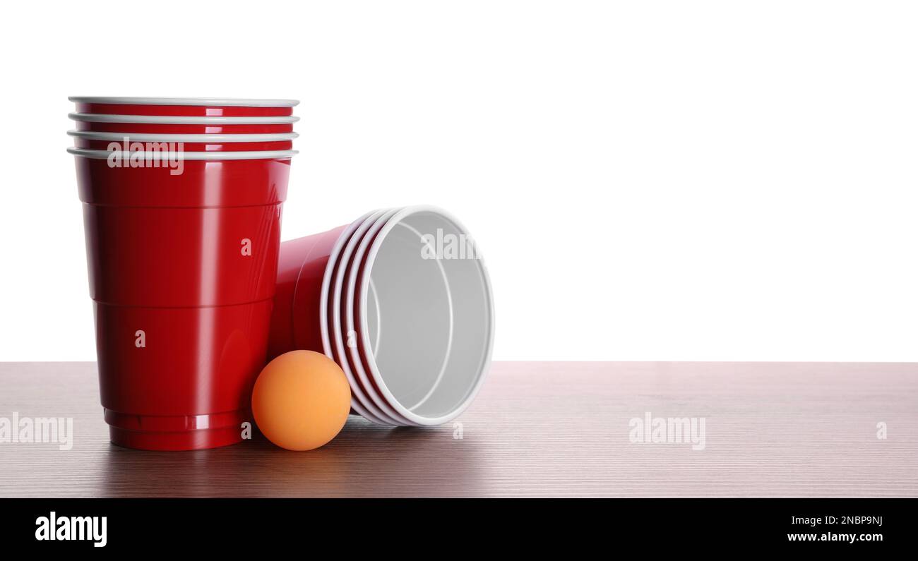 Plastic cups and ball for beer pong on wooden table against white ...