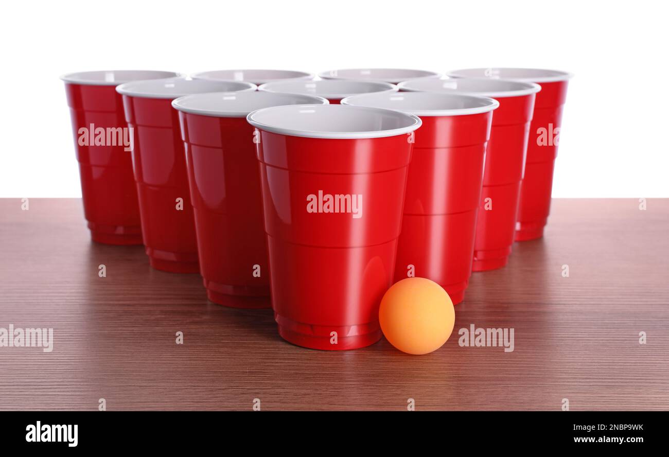 Plastic cups and ball for beer pong on wooden table against white ...