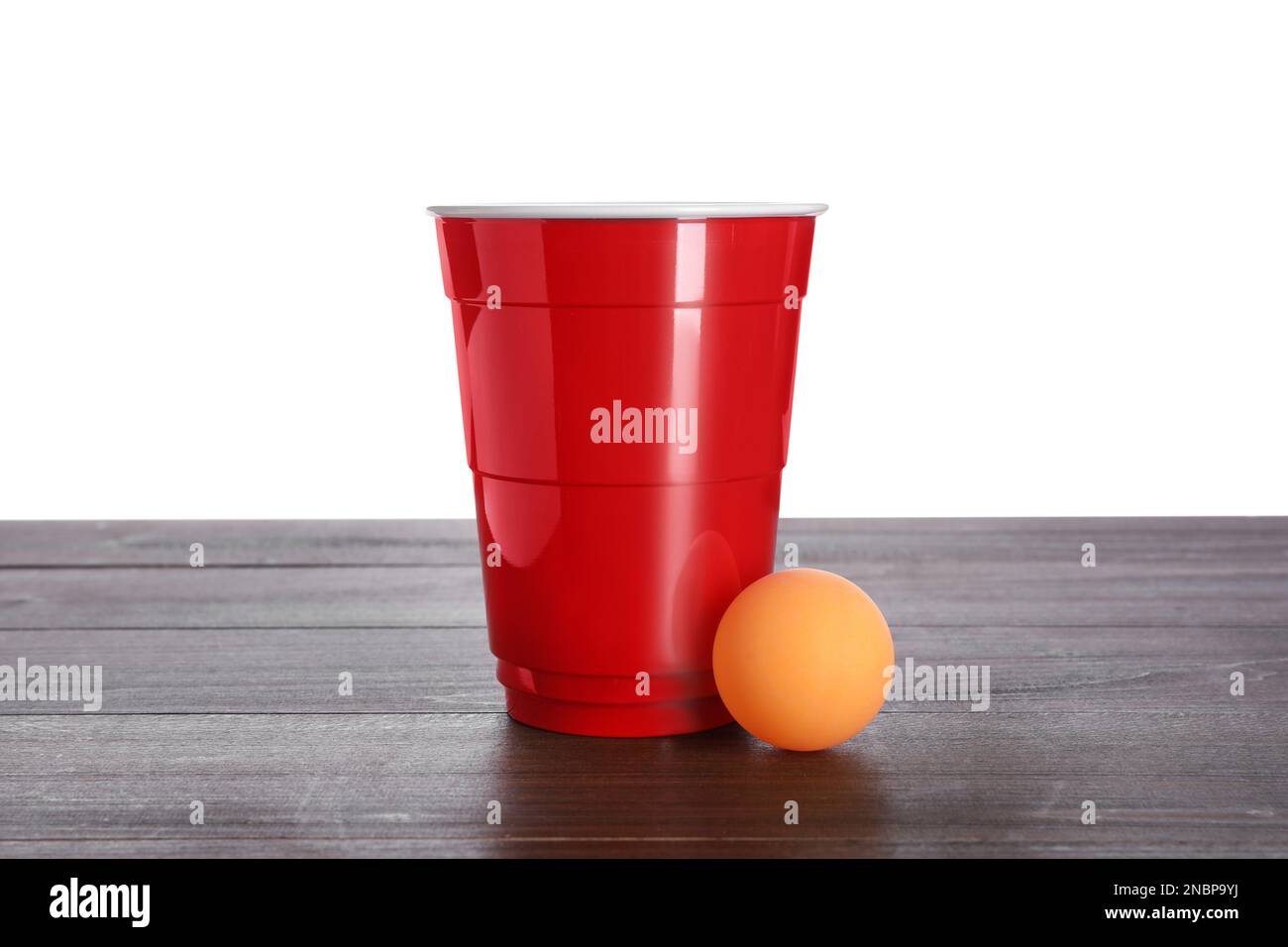 Plastic cup and ball for beer pong on wooden table against white ...