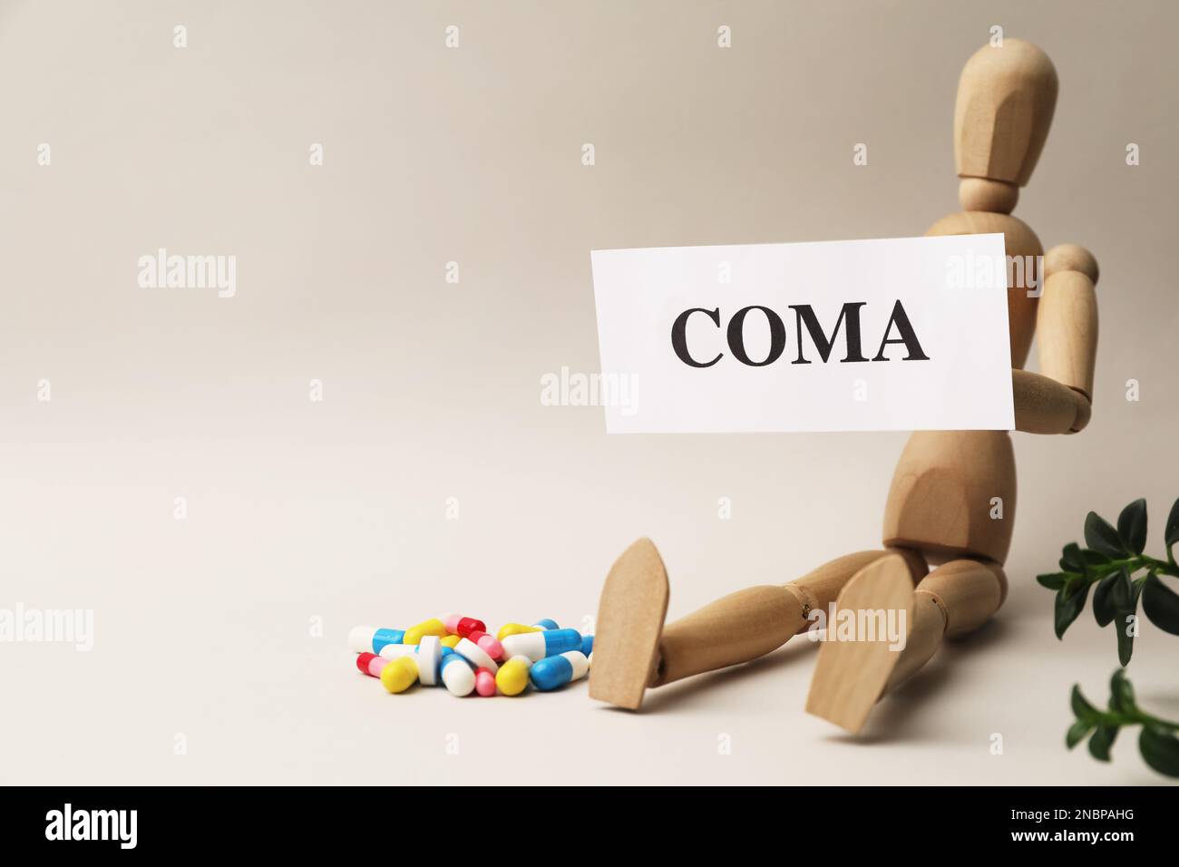Human mannequin holding card with word Coma and pills on beige ...