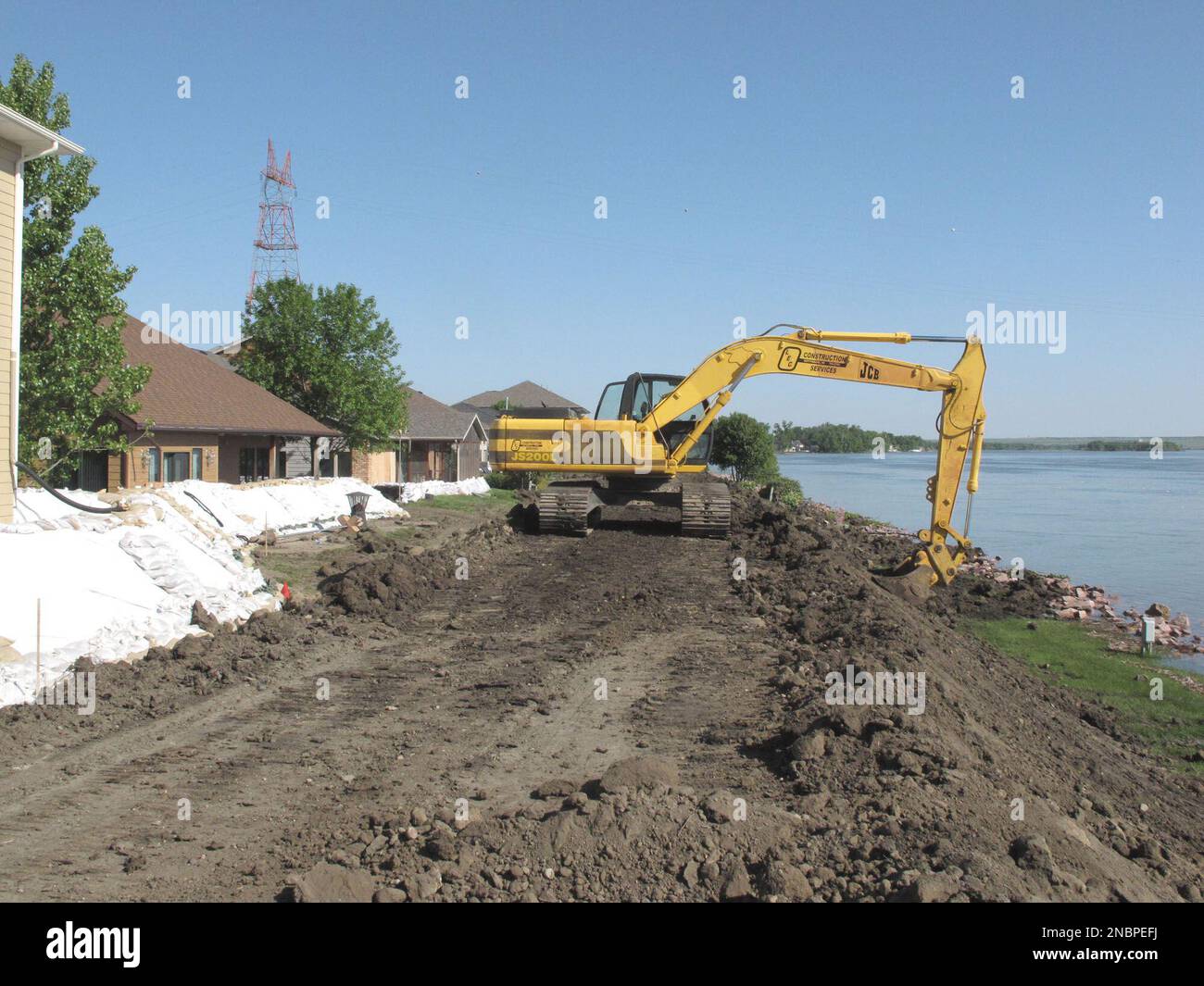 A backhoe shapes the side of a flood-control levee being built ...