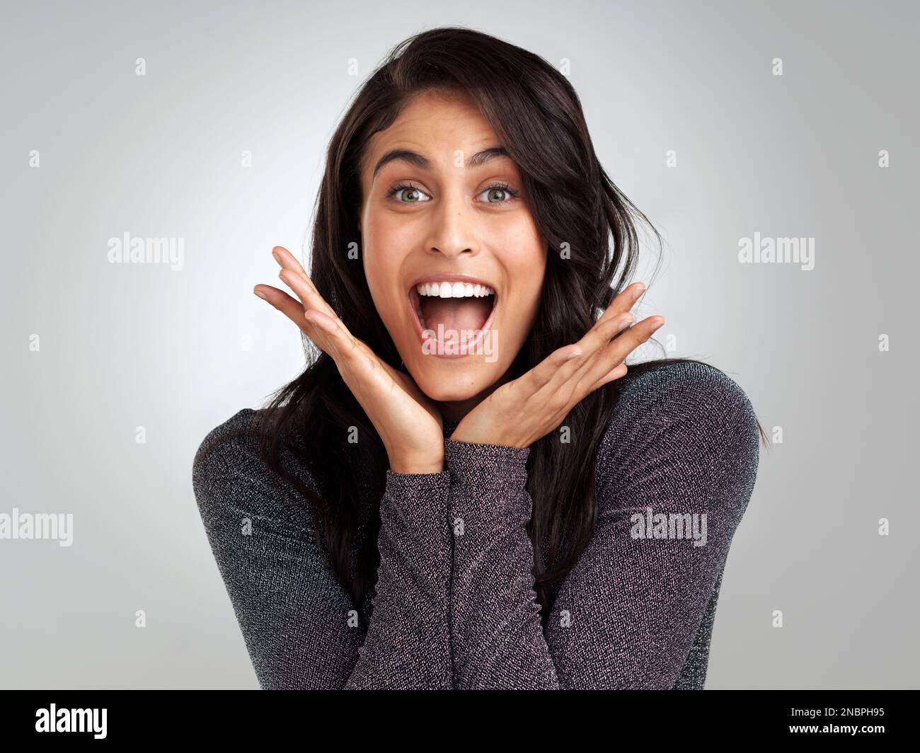 Im really excited about this. a young woman looking surprised while standing against a grey ...