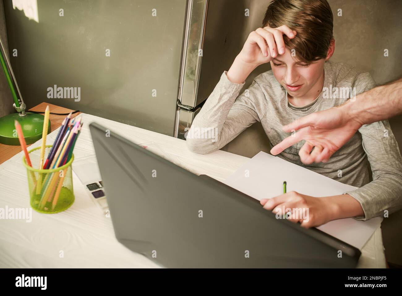 The boy writes down the task on a blank sheet lying near the laptop ...