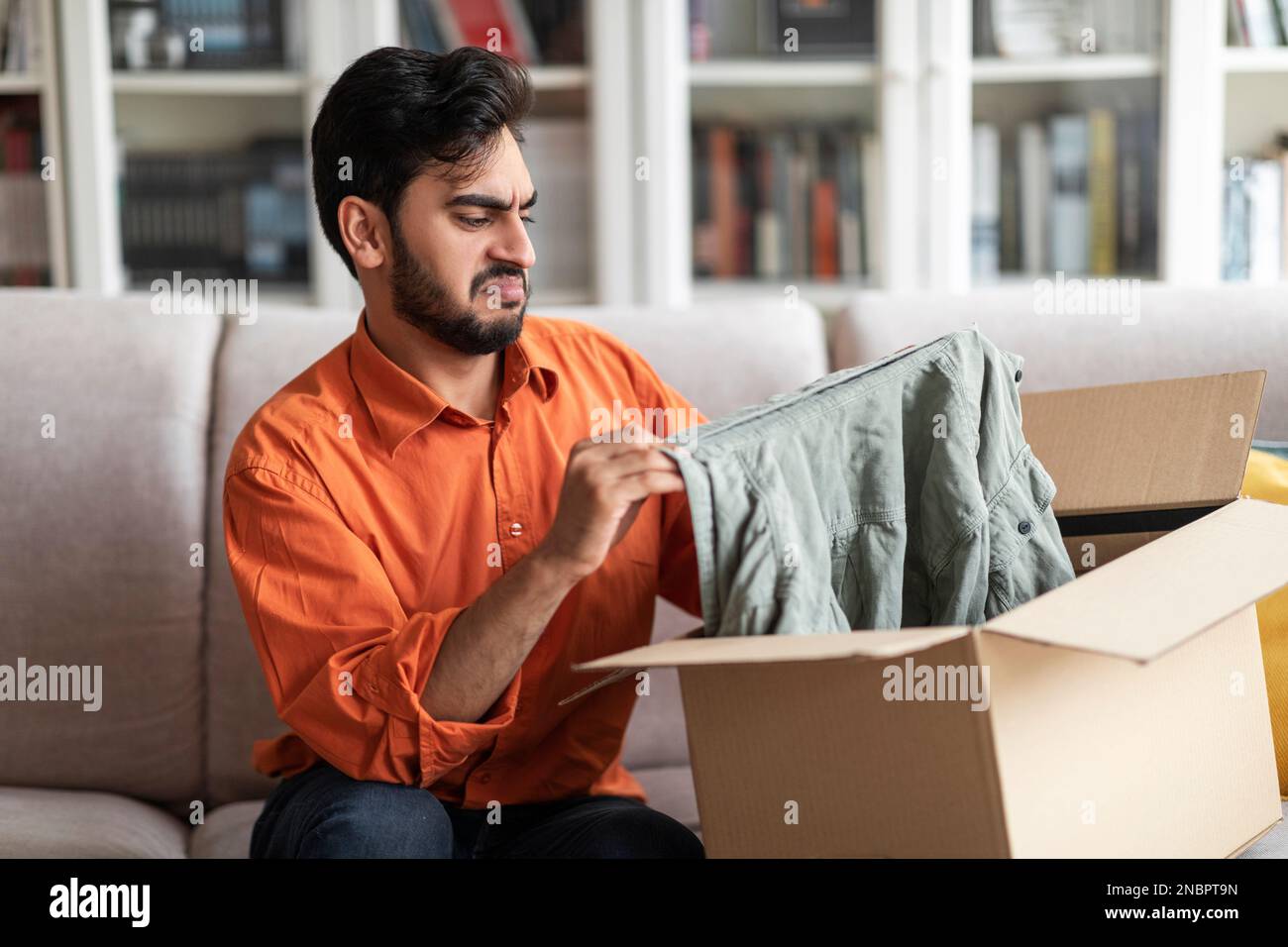 Disappointed middle eastern man customer opening parcel at home Stock ...