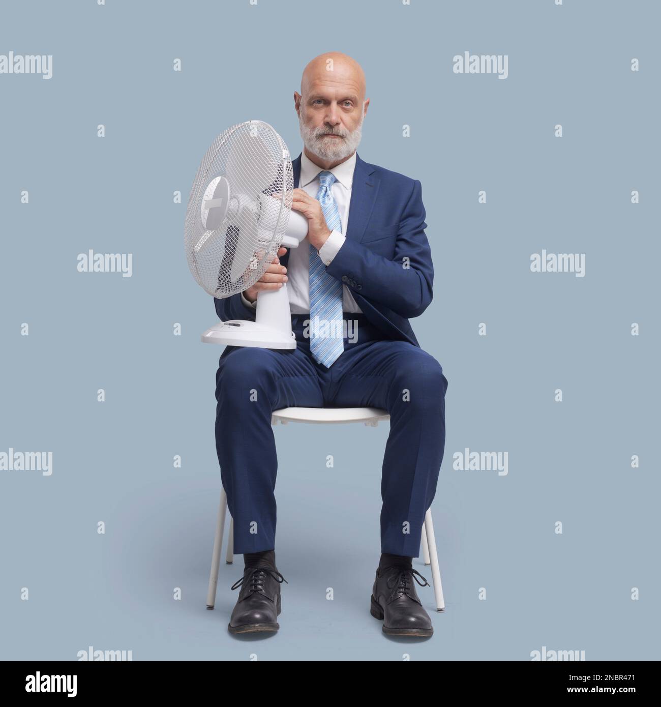 Man sitting and holding an electric fan, isolated on gray background ...