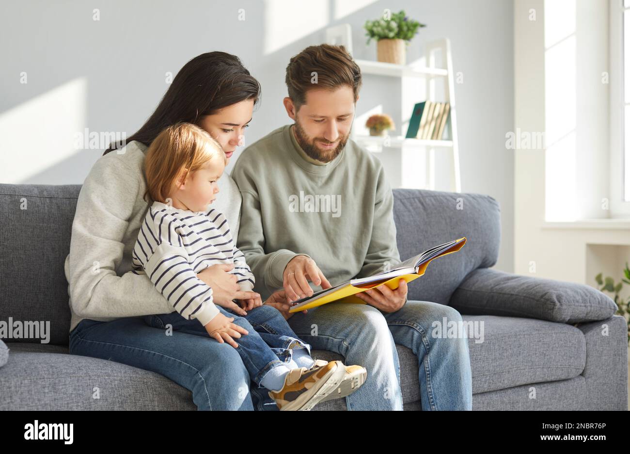 Parents and their adorable toddler baby reading book Stock Photo - Alamy