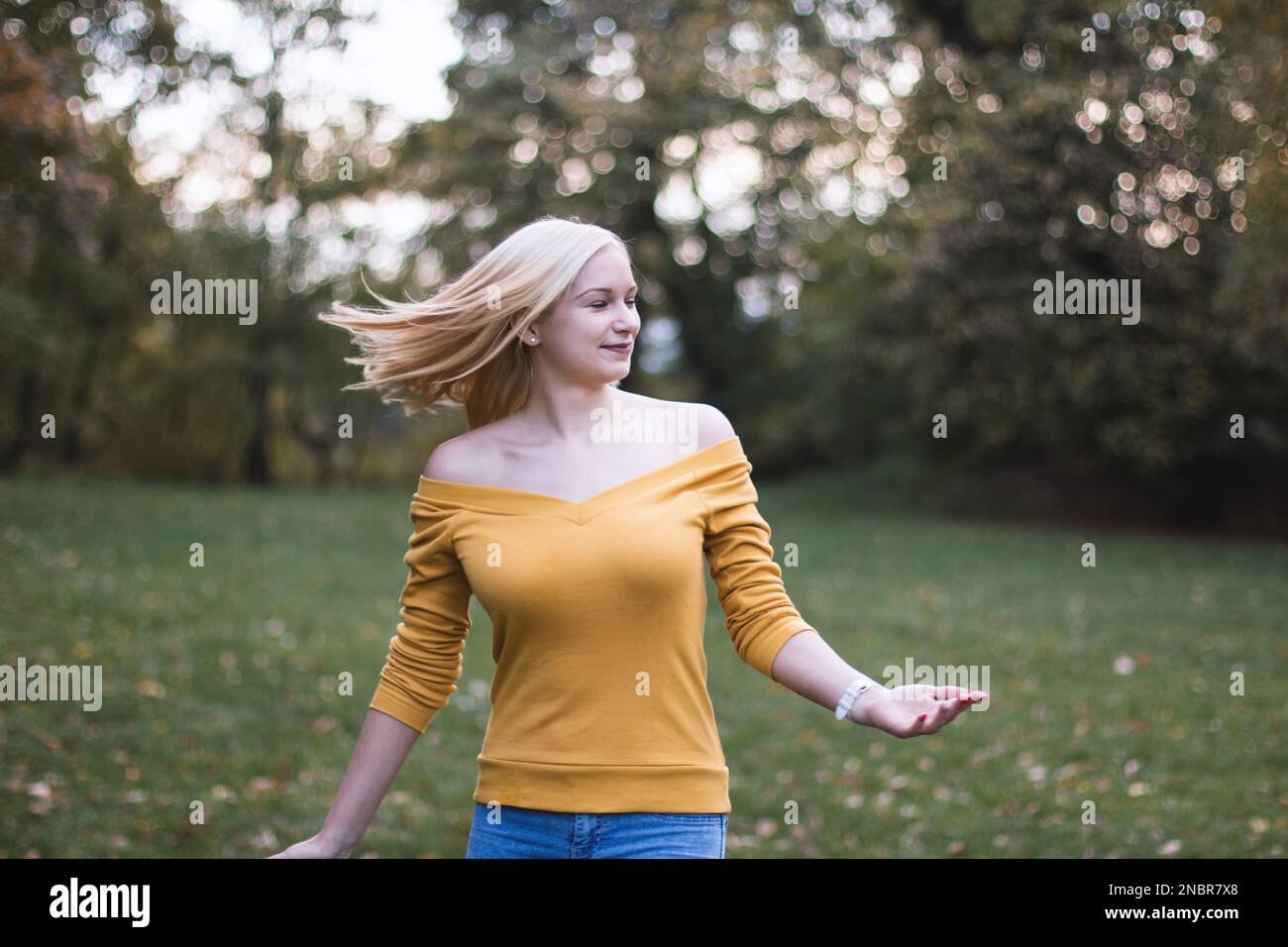 Young blonde woman dancing freely alone in the park, turning around ...