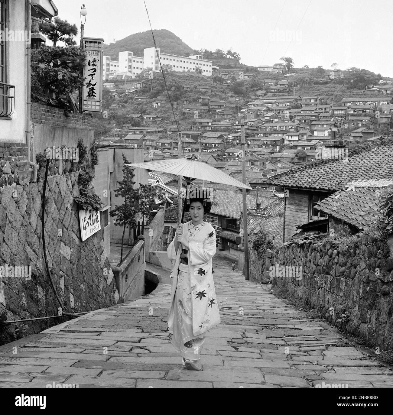 Carrying a parasol, and wearing traditional garb, a Japanese girl walks ...