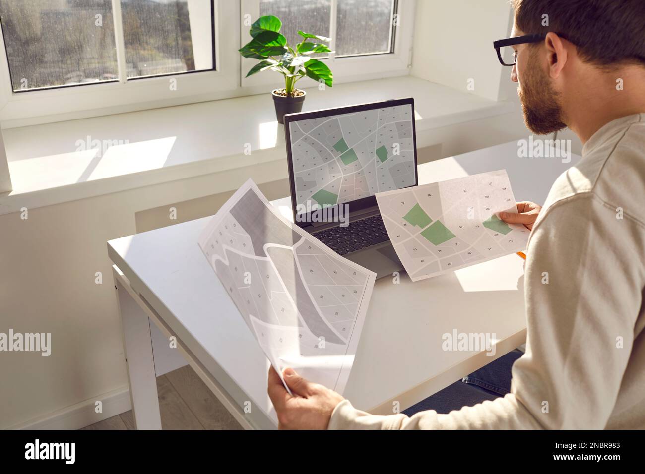 Serious engineer with cadastral maps and projects is sitting at desk ...