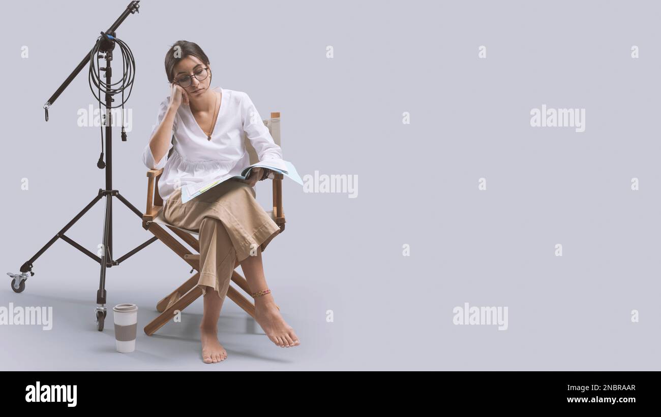 Focused film director sitting on the director's chair and reading a ...
