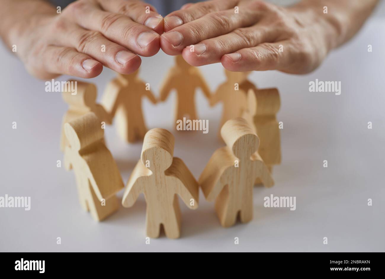 Insurance agent's hands protect wooden figures of people standing in ...