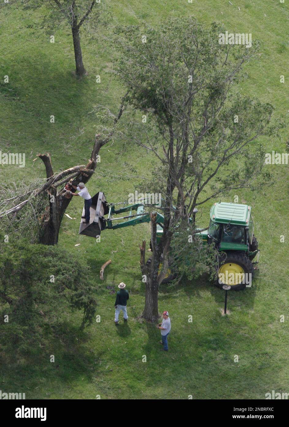 A man trims a tornado damaged tree from the loader of a farm tractor ...