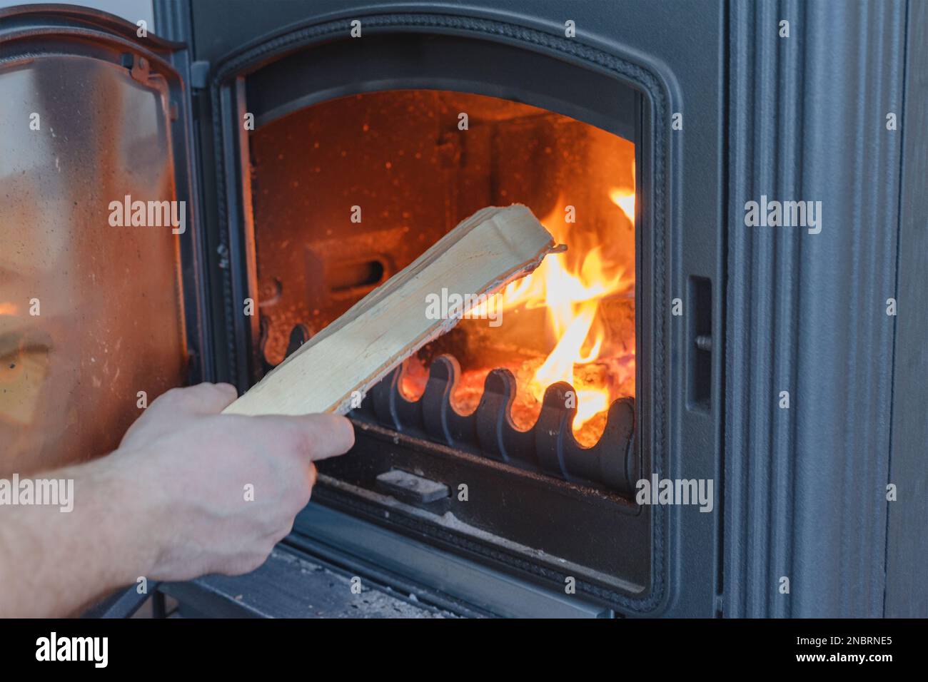 A man throws wood in the fireplace. Open cast-iron stove-fireplace with ...