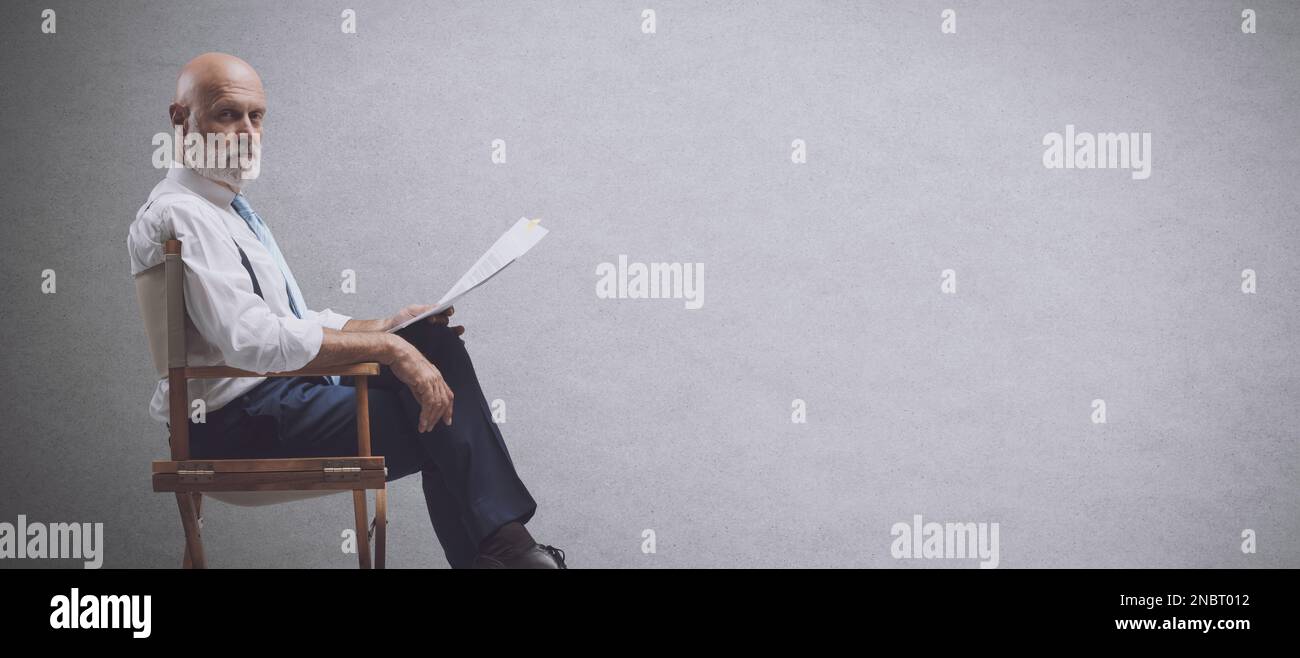 Professional filmmaker sitting on the director's chair and holding a ...