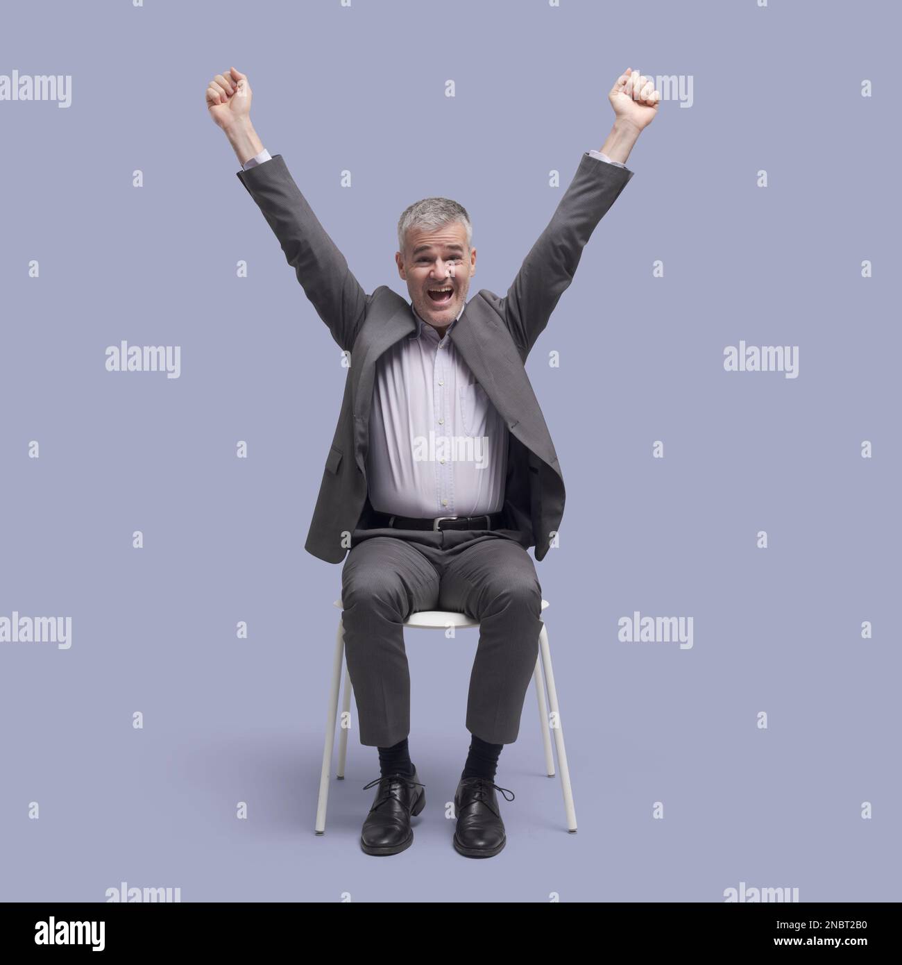 Happy successful man sitting on a chair and celebrating with raised ...