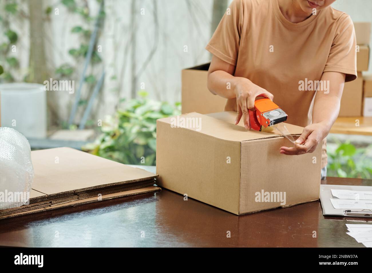 Woman packing orders and sealing cardboard boxes for delivering to ...