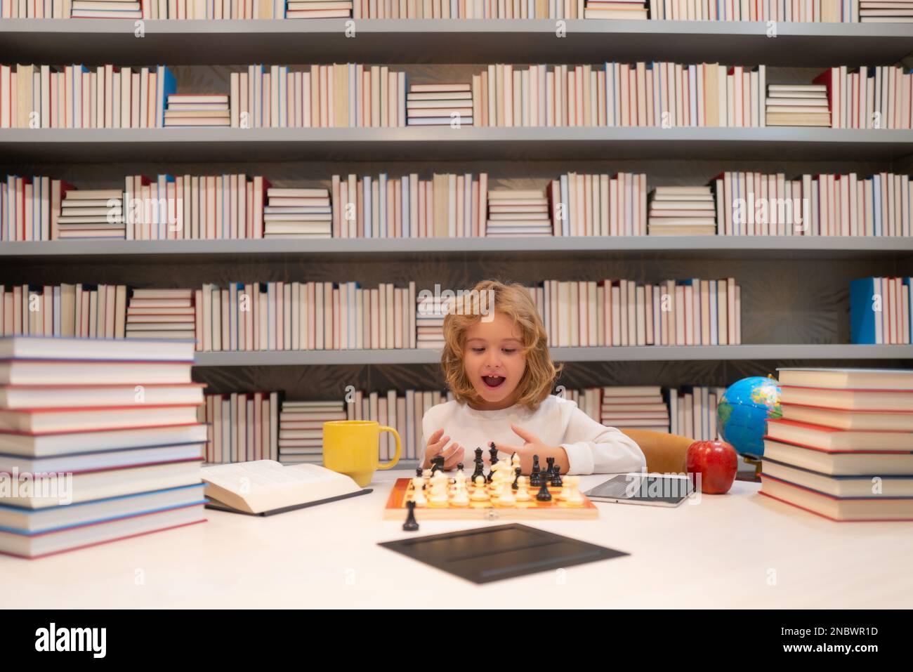 Early development. Smart boy play chess in the library by the ...