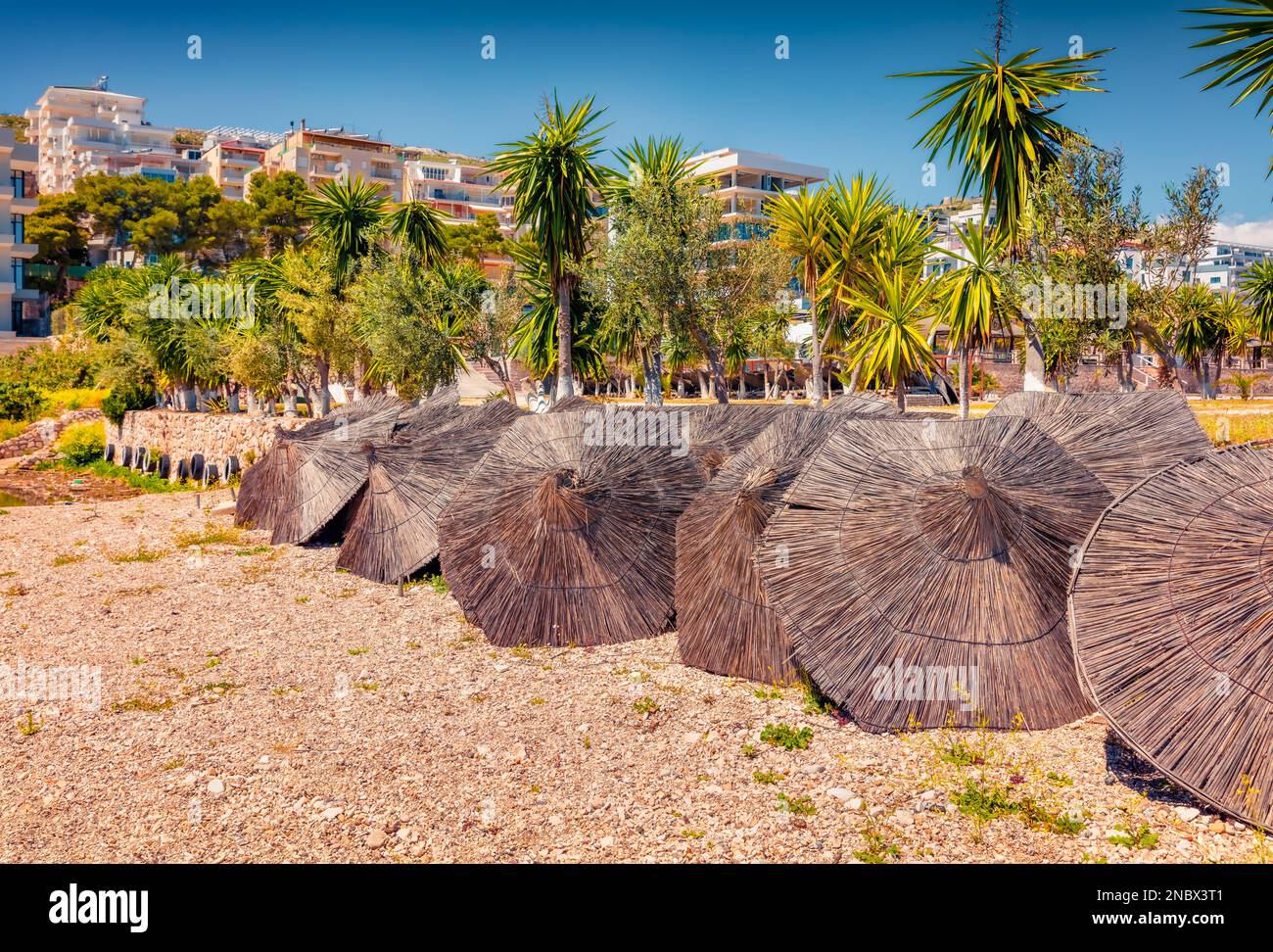 First warm days in Saranda resort. Straw umbrellas on the shore of ...