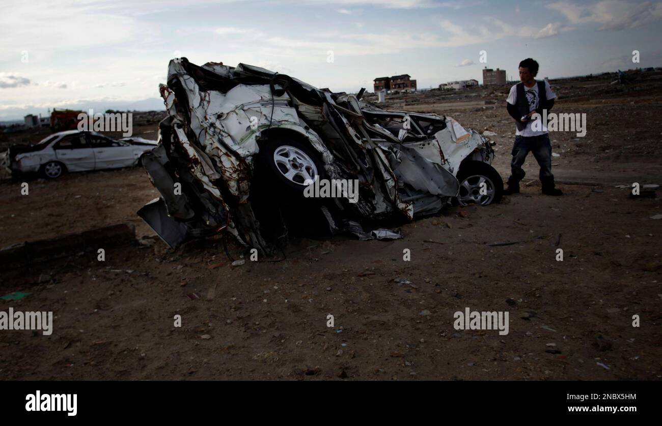 A man watches a totally wrecked car in an area destroyed by the March ...