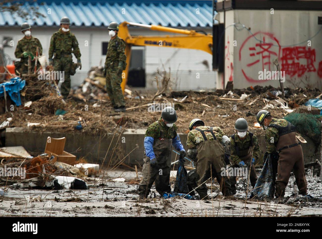 Japan Ground Self-Defense Force members try to pick up tarps from mud ...