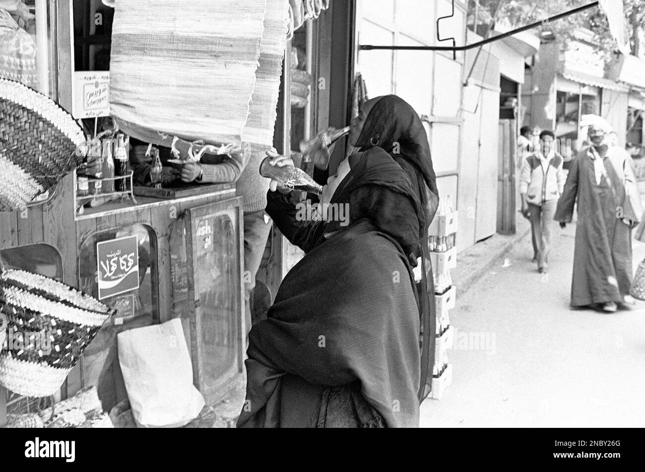 Two Egyptian village women dressed in the traditional black robes drink ...
