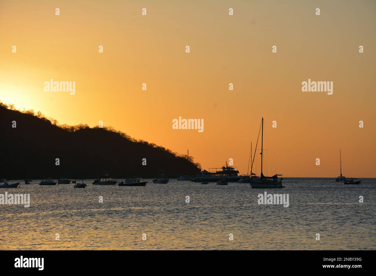 Costa Rican sunset on Playa de Coco, with mountain and booats on water ...