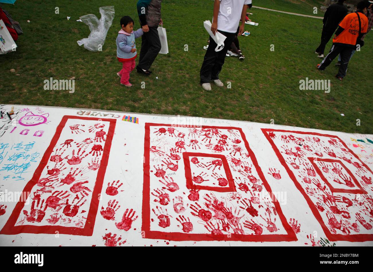 A child walks past a painting of the number 100 and red hand prints ...