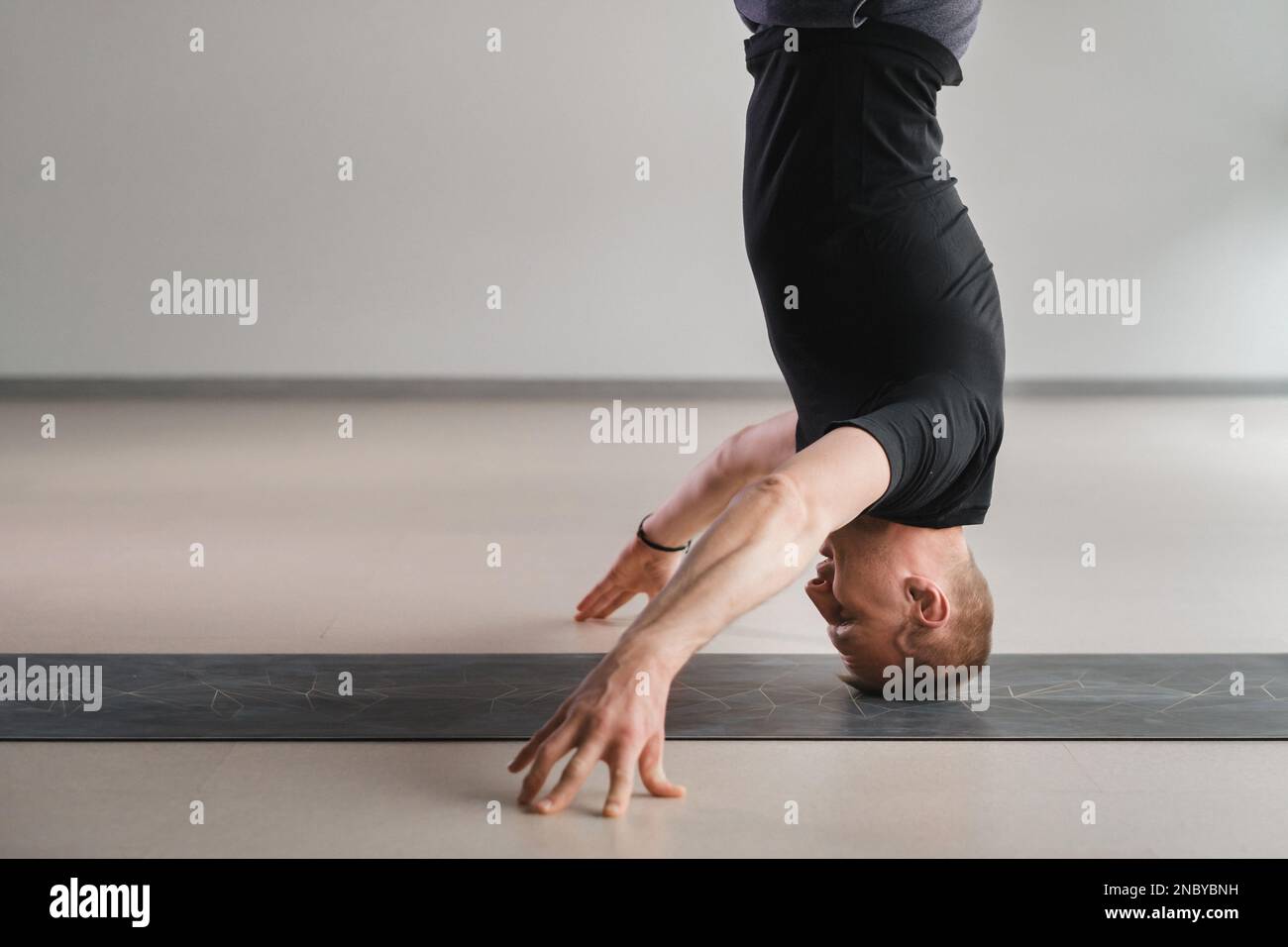 A man performs a yoga pose with support on his head in the gym. Yogi in ...