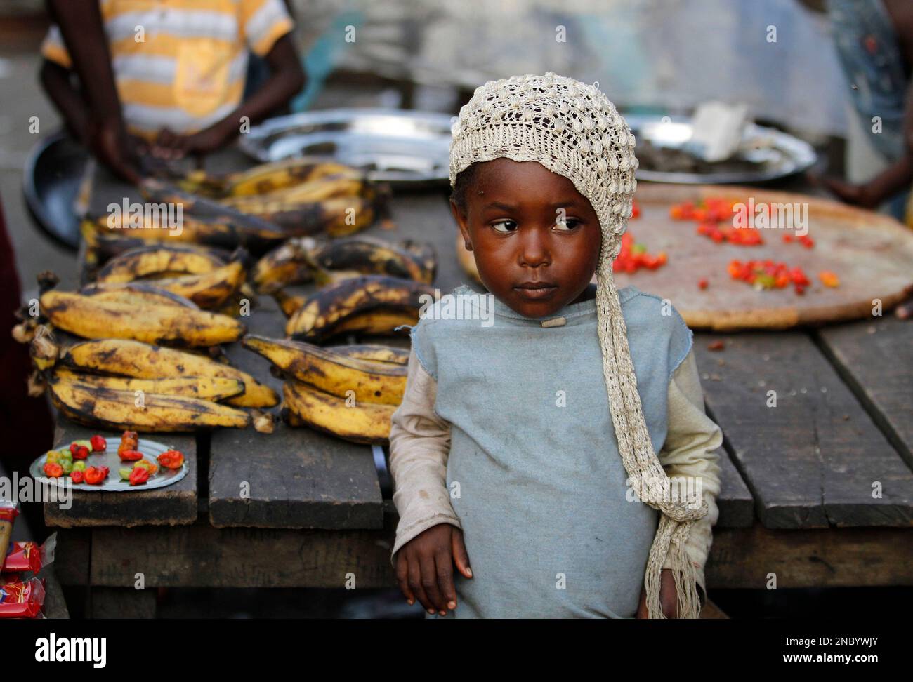 Fanta Bamba, 3, leans on her mother's fruit and vegetable stand, in a ...