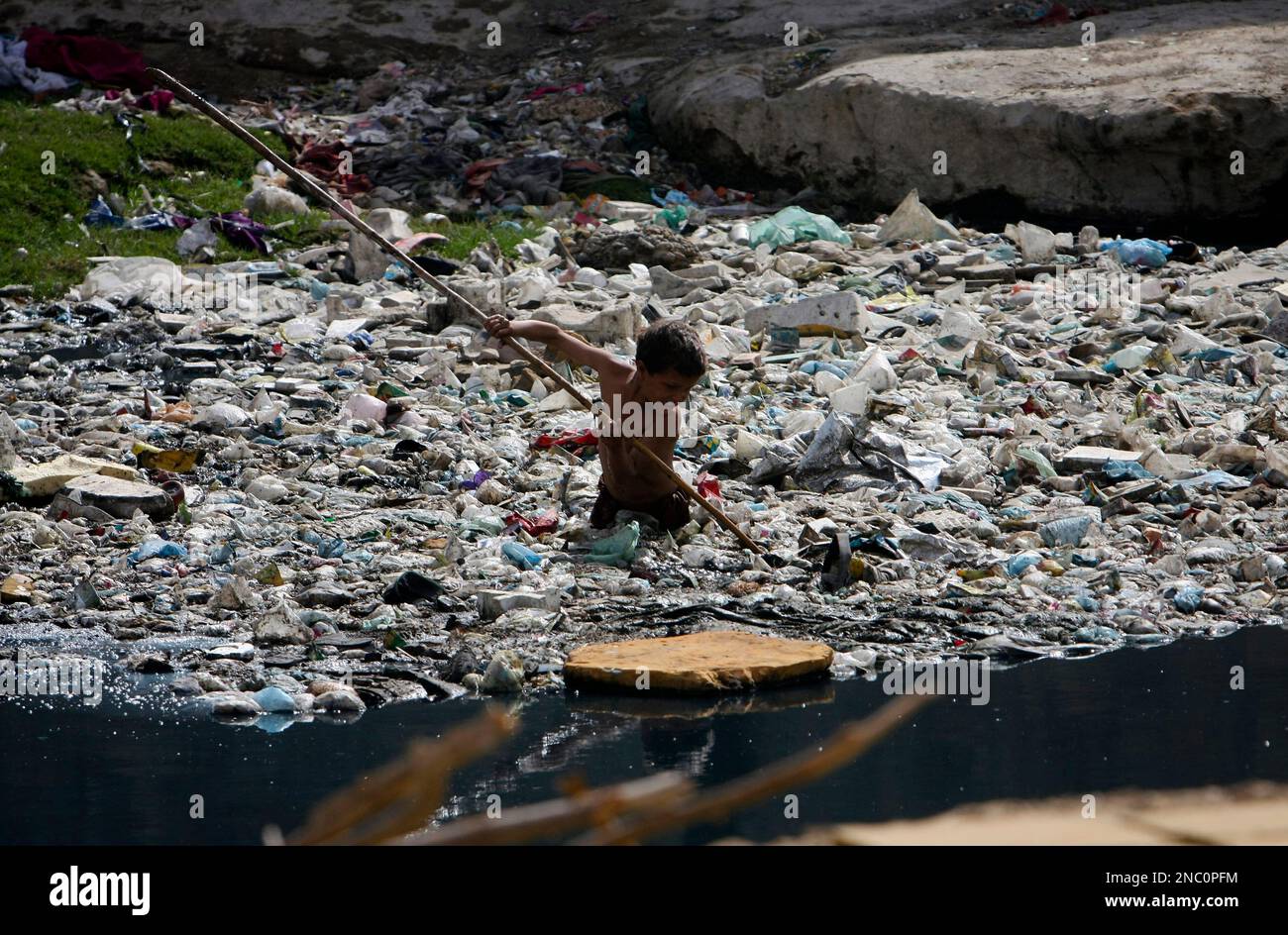 A Pakistani boy searches for recyclable items through a pile of waste ...