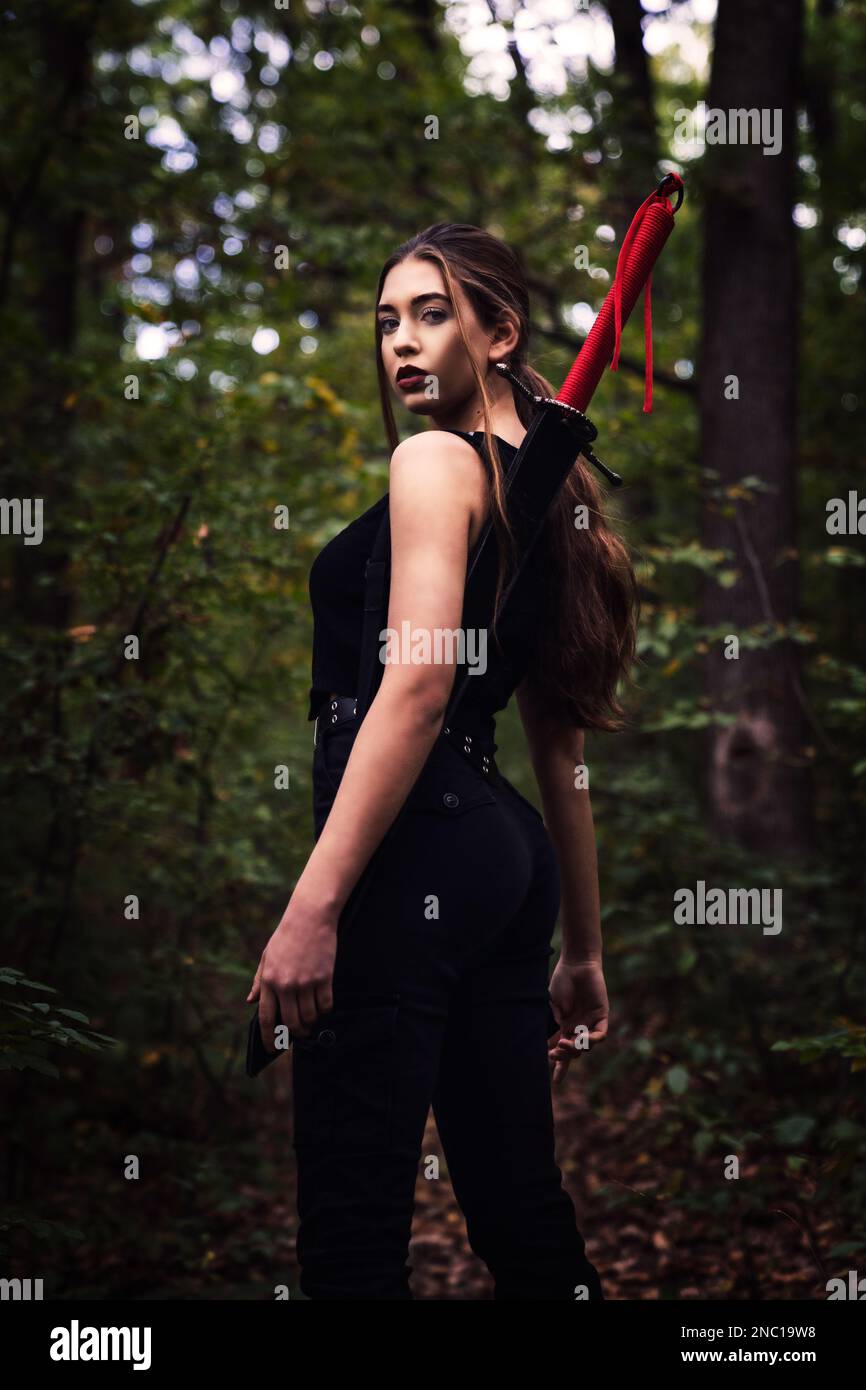 A low-angle of a female in black costume holding a sword on the ...