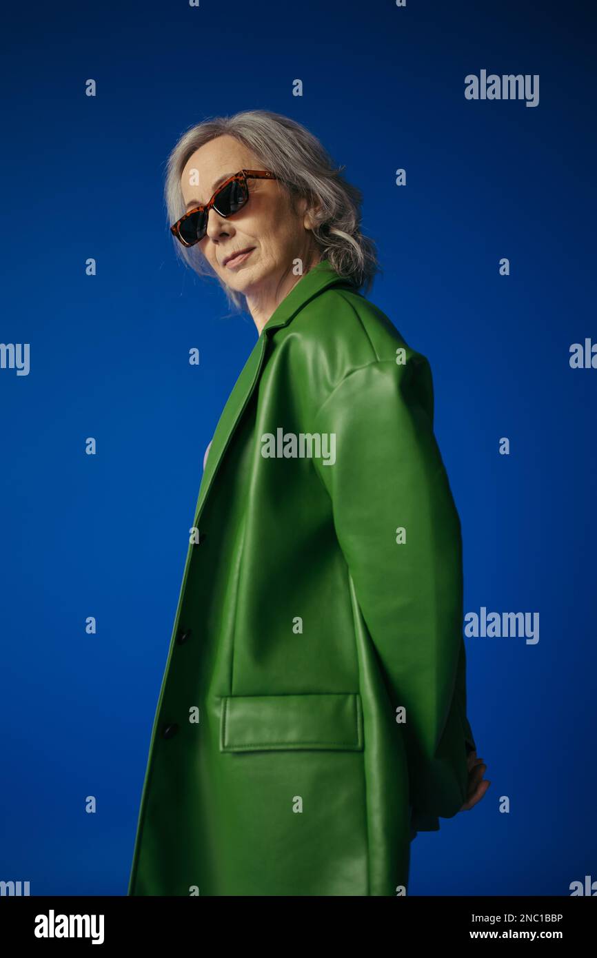 senior model in stylish sunglasses and green leather jacket posing ...