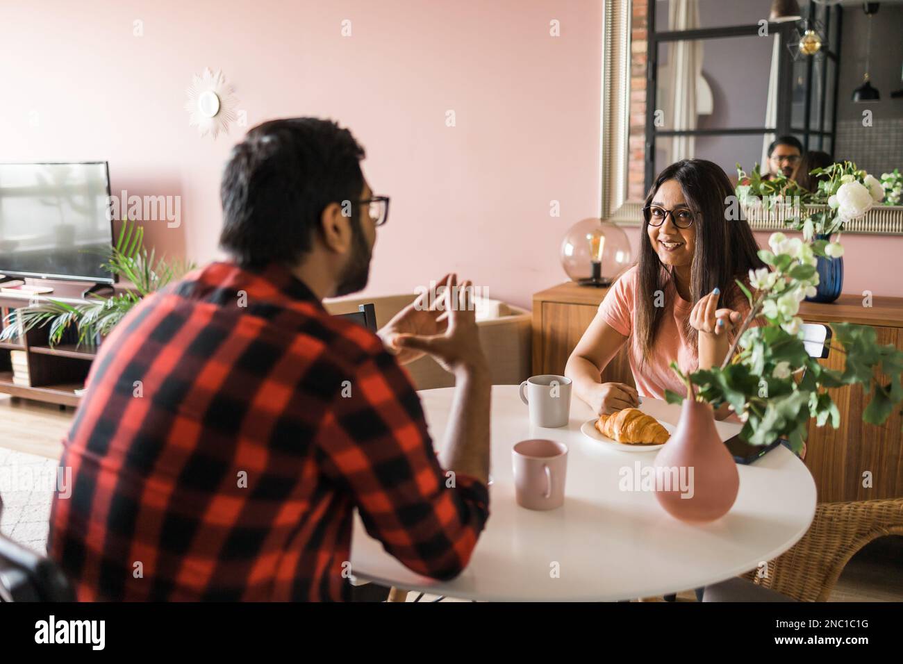 Happy indian couple having breakfast and small talk together in the kitchen - friendship, dating ...