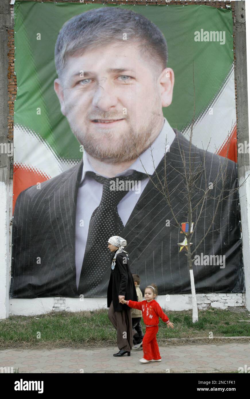 A woman with children walks past a huge poster with a portrait of ...