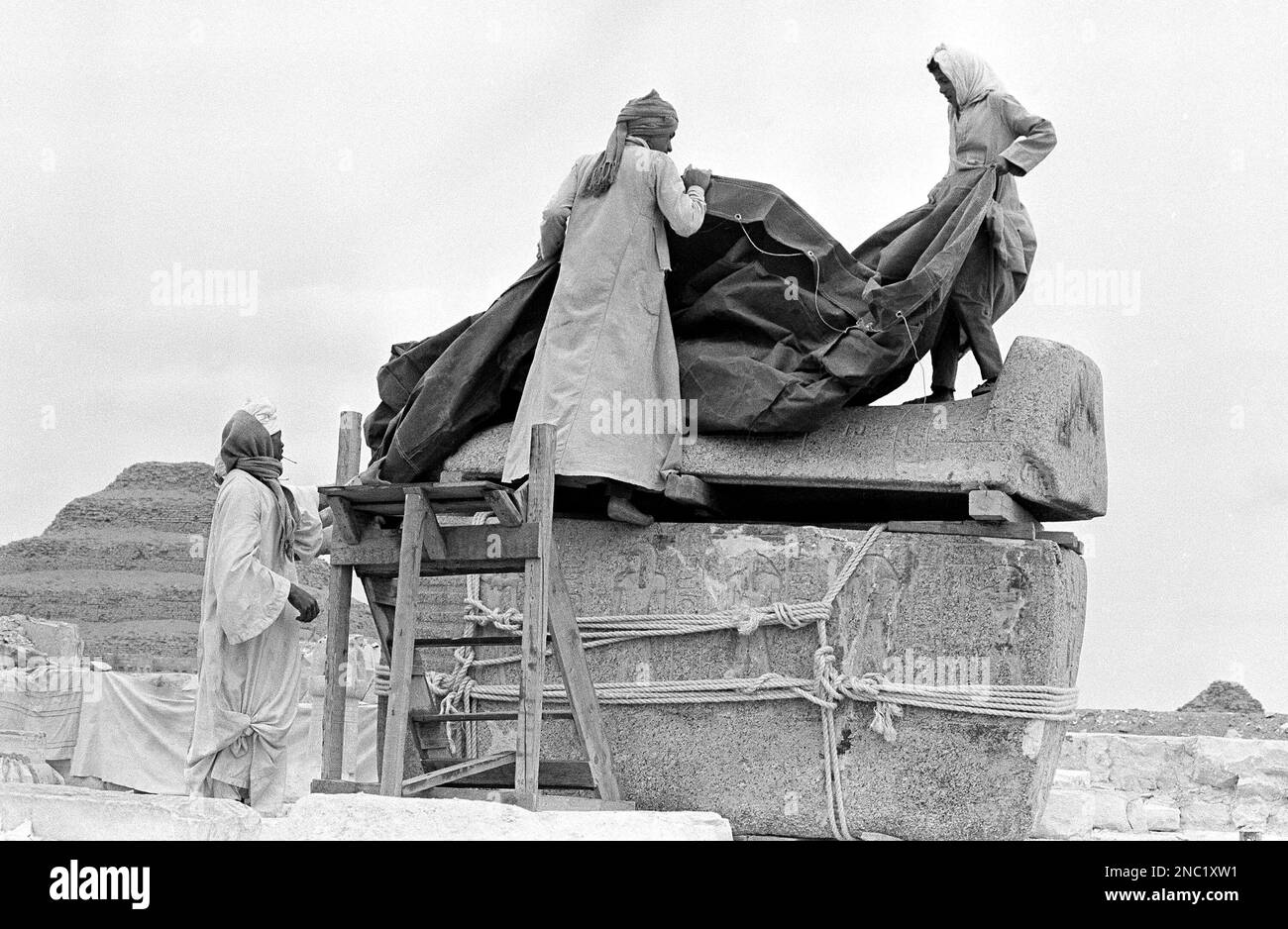 Workmen remove a canvas covering from a sarcophagus of Nefer-renpet, a ...