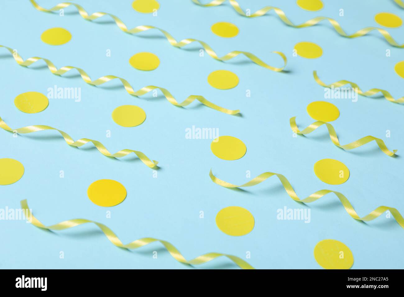 Shiny yellow serpentine streamers and confetti on light blue background ...