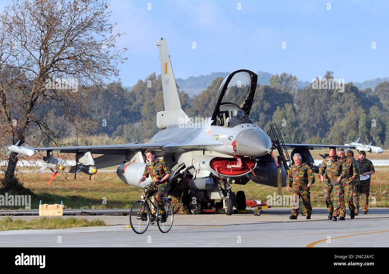 A soldier on a bicycle rides by a Belgian F-16 fighter jet at Araxos ...